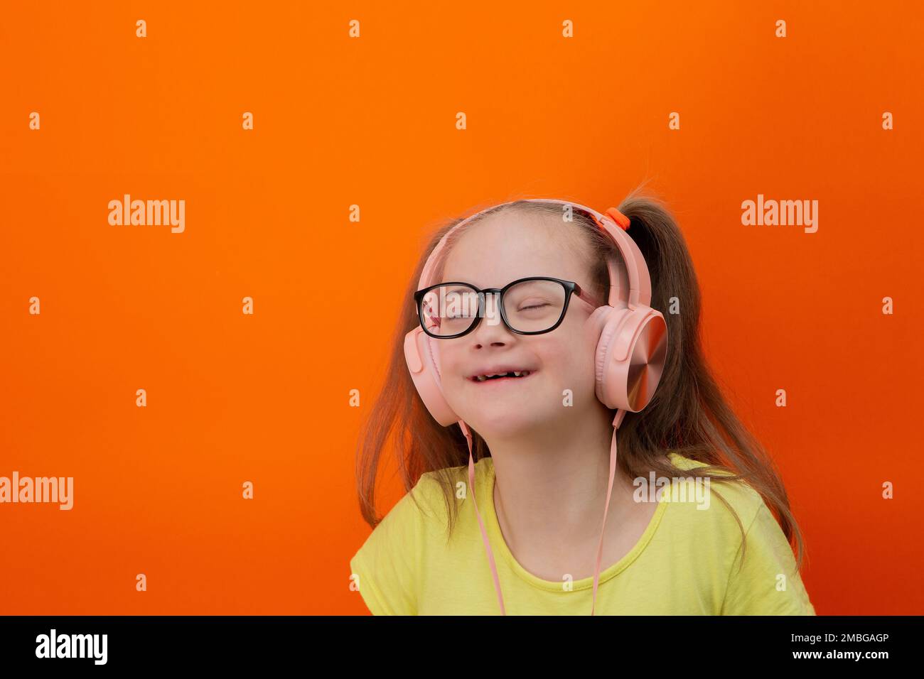 Girl with Down syndrome listens to music. Orange background Stock Photo - Alamy
