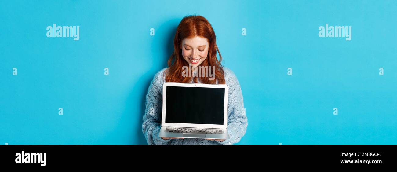 Cute redhead woman in sweater, showing and looking at laptop screen ...