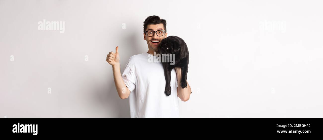 Happy and satisfied dog owner showing thumb-up, holding cute black pug ...