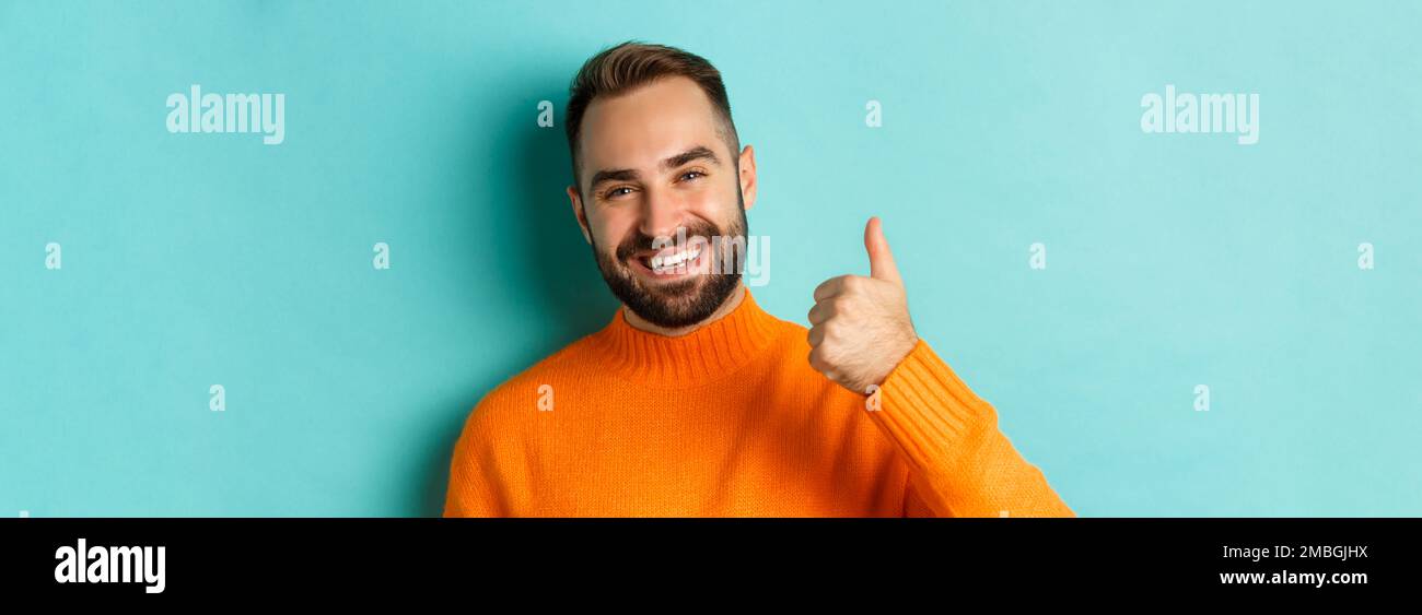 Close-up of attractive young man showing thumb-up, praising good work ...