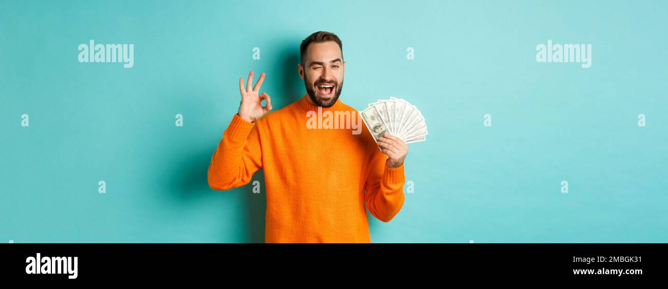 Shopping. Excited guy holding money, showing ok sign and winking ...