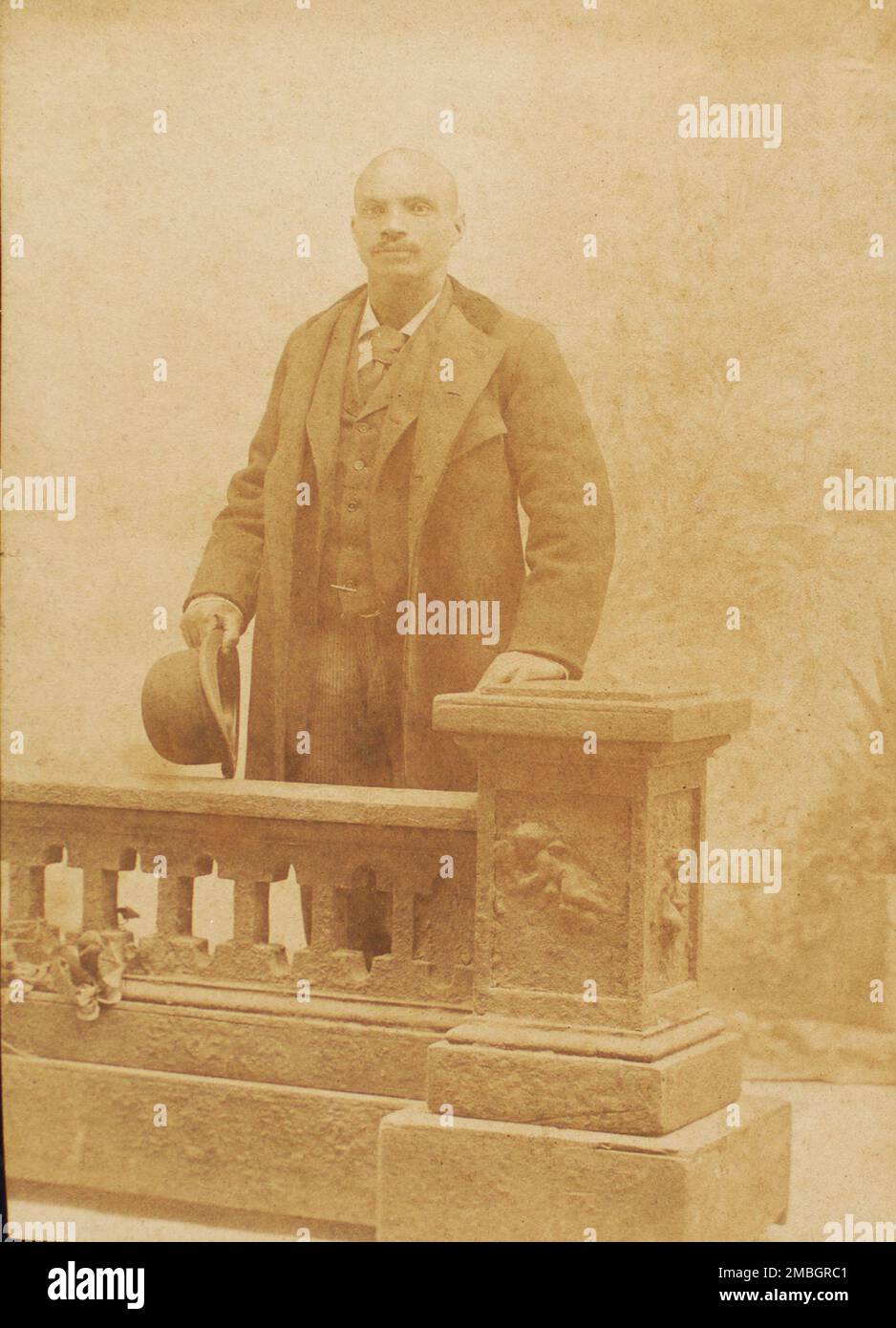 Studio portrait of man dressed in suit and coat, holding bowler hat ...