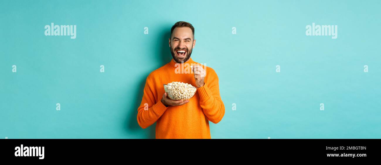Excited young man watching interesting movie on tv screen, eating ...