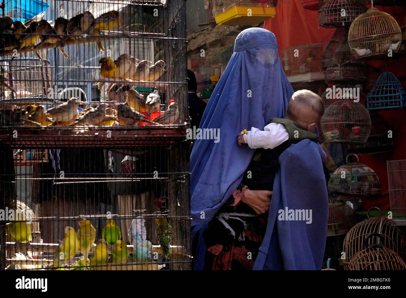 A woman wearing a burka walks through a bird market as she holds her ...
