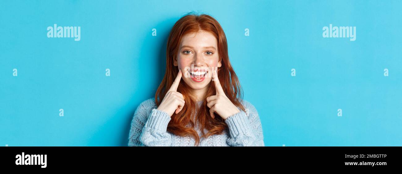 Close-up of cheerful teenage girl with red hair and freckles, poking ...