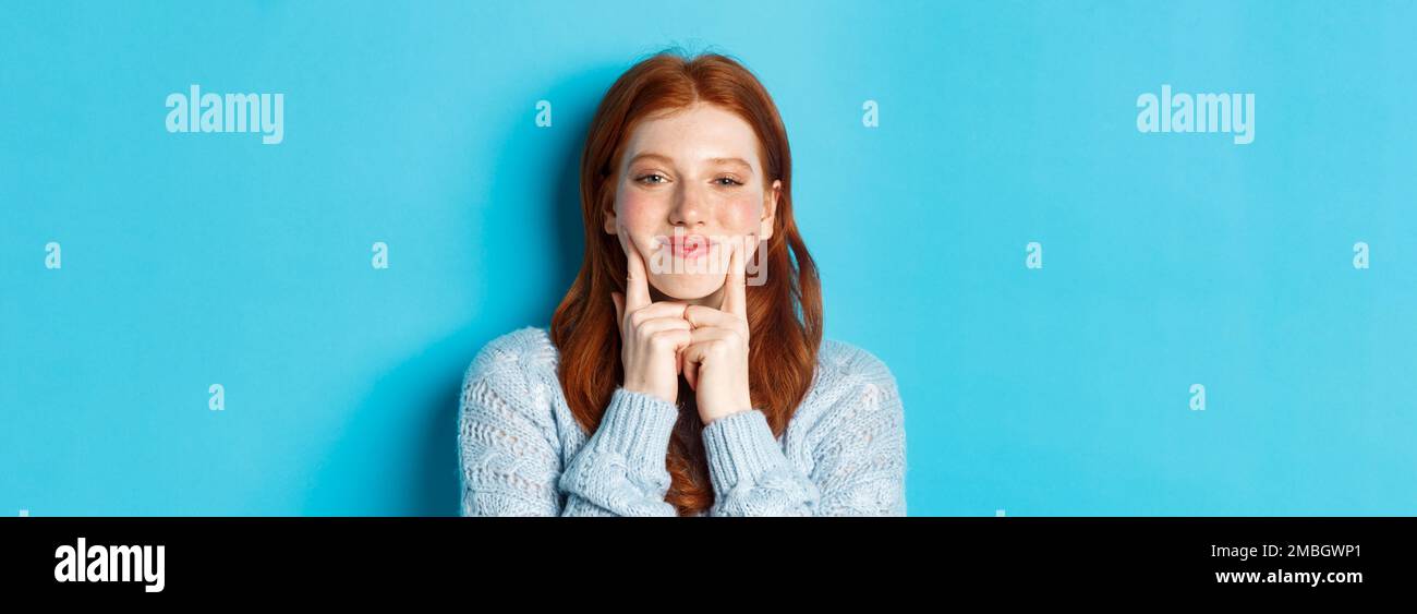 Close-up of cute and silly girl with red hair poking cheeks, showing ...