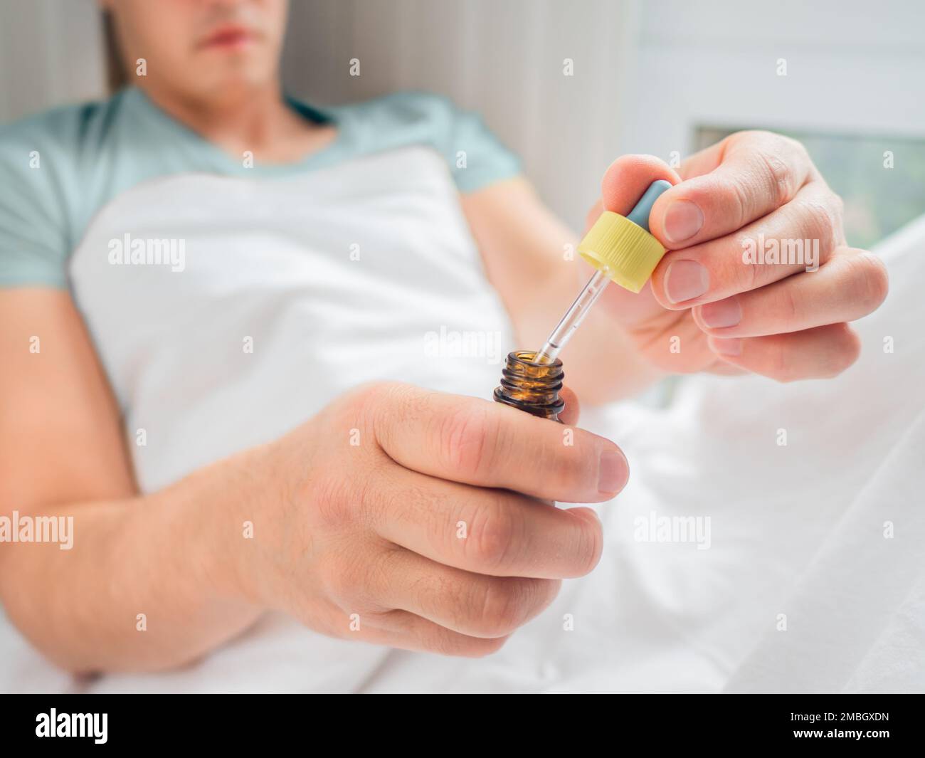 Ill man is lying in bed with liquid medicine. Man is measuring drops ...