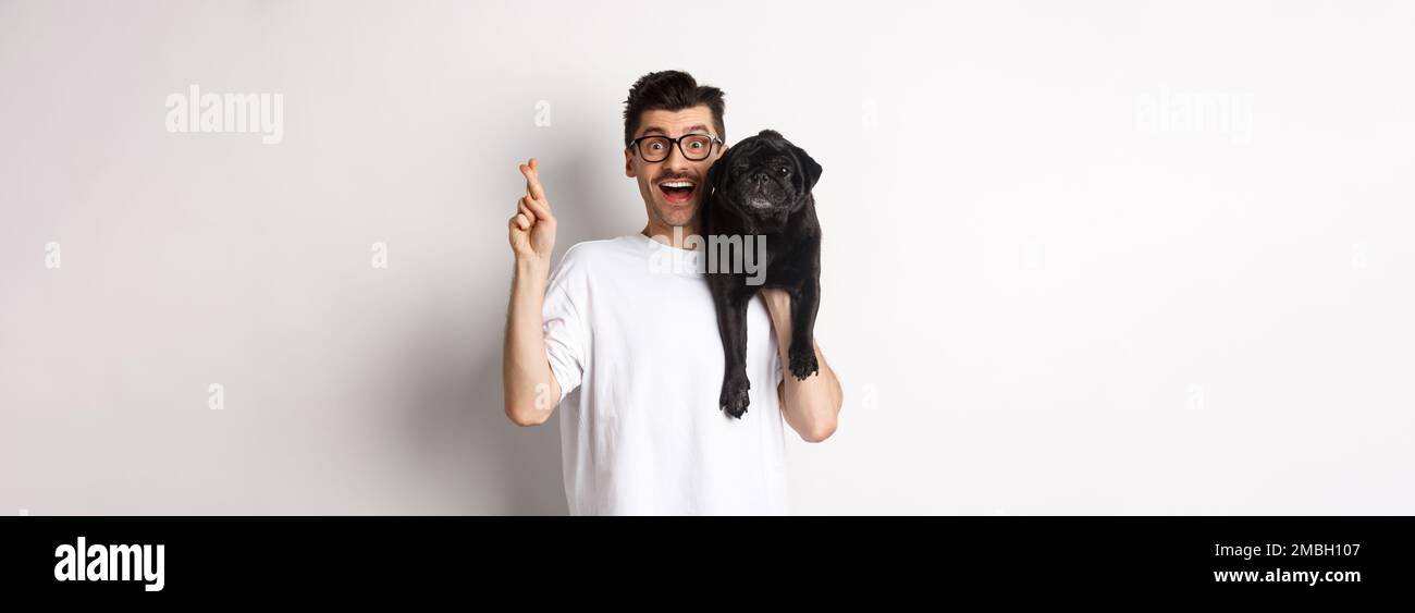 Hopeful smiling dog owner making a wish, holding cute black pug on ...