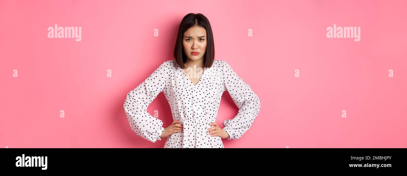 Cute offended girl frowning, holding hands on waist and staring at ...