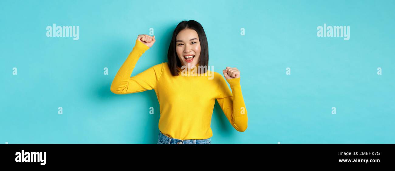 Cheerful asian woman partying, having fun and dancing over blue ...