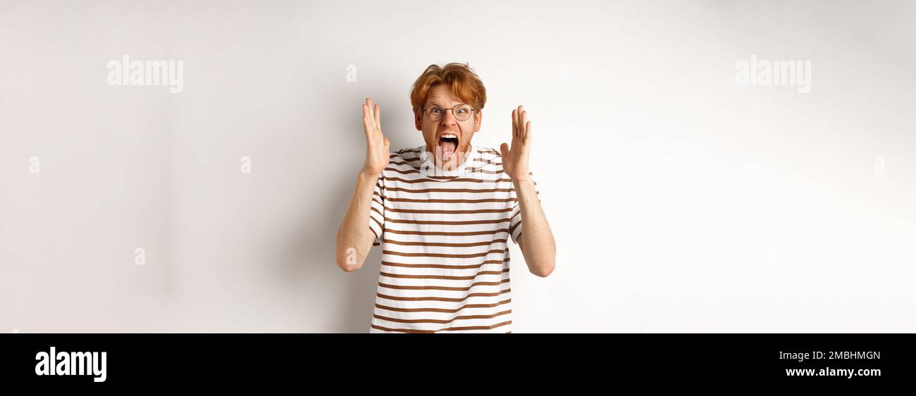 Angry young man with red hair shouting at camera, screaming and looking ...