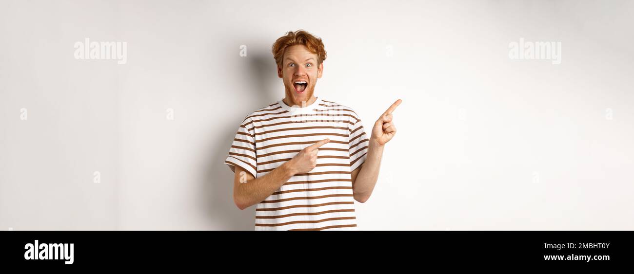 Cheerful man with red hair checking out promo offfer, pointing left at ...