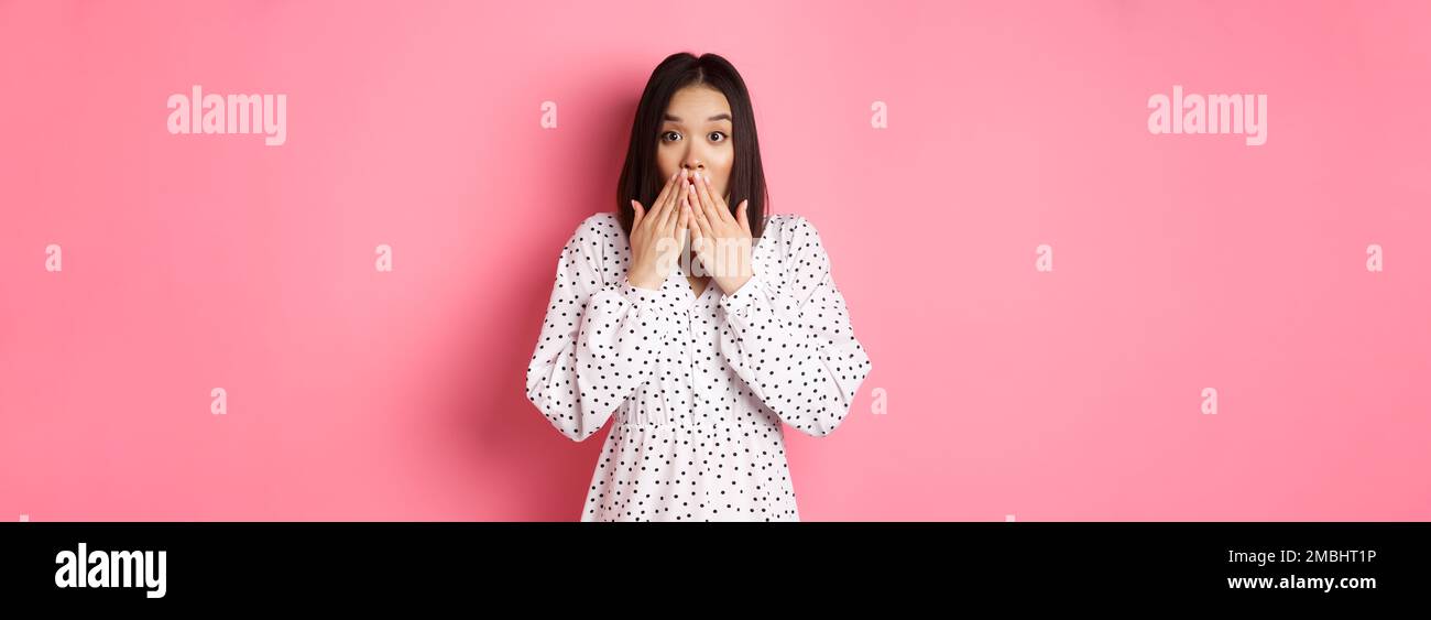 Worried asian girl in dress looking concerned, cover mouth and gasping ...