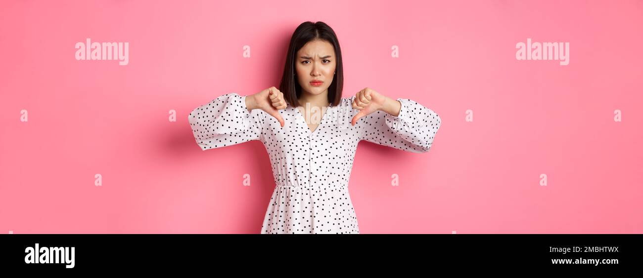 Disappointed asian woman showing thumbs-down, disapprove and dislike ...