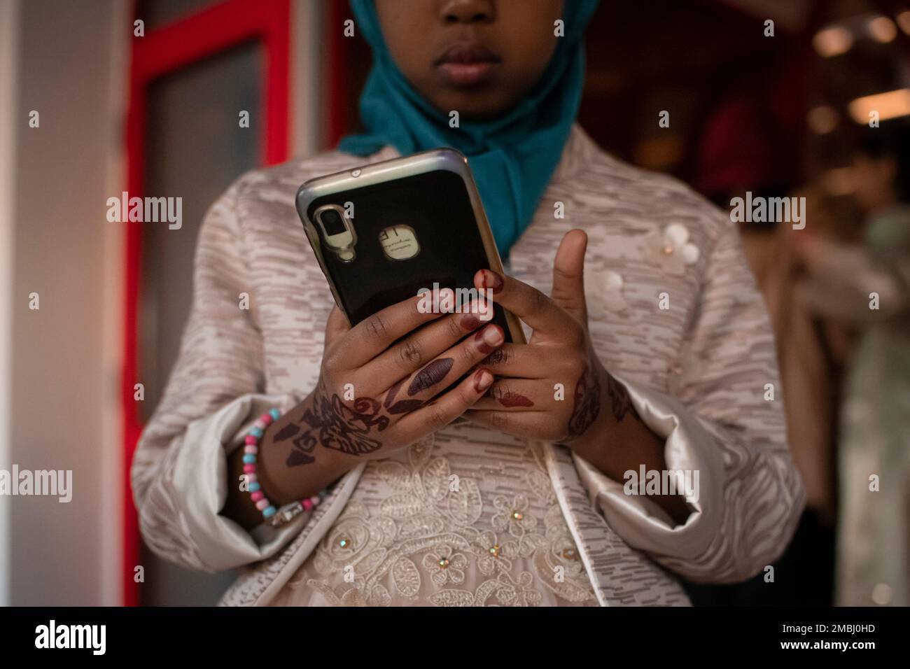 A girl with henna tattoos on her hands holds a mobile phone during Eid ...
