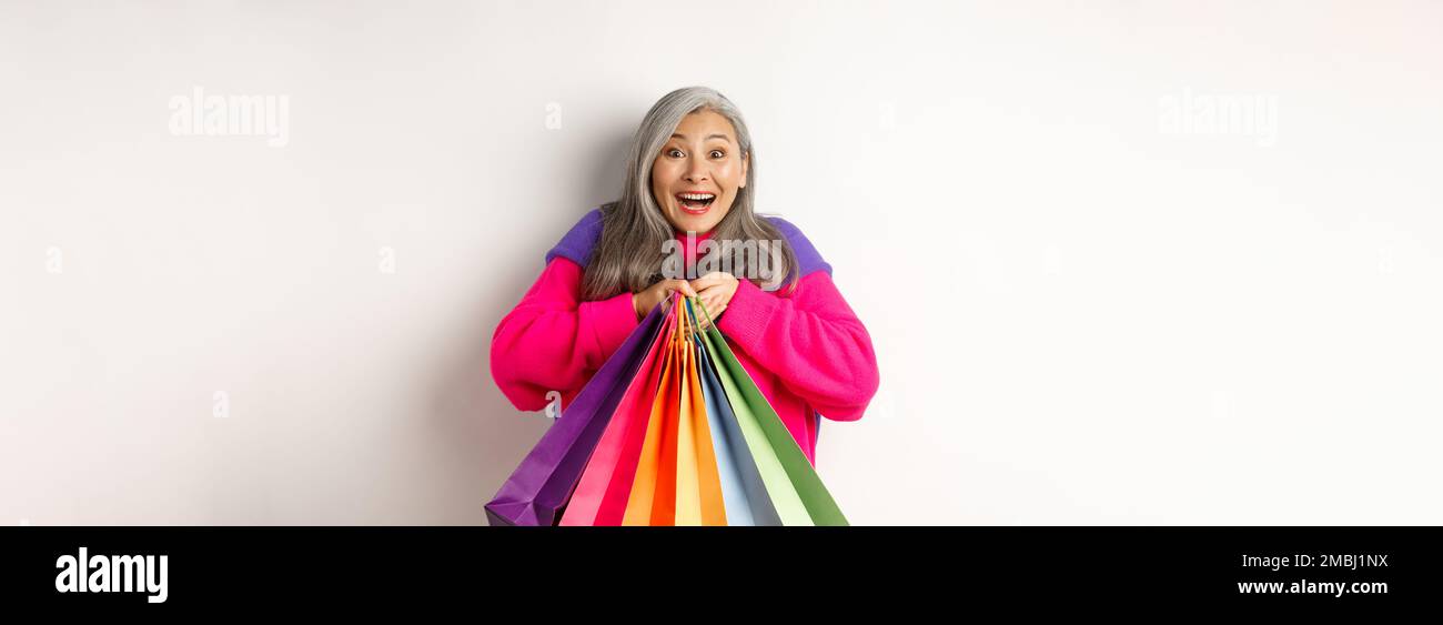 Fashionable senior asian woman shopaholic, hugging shopping bags and ...
