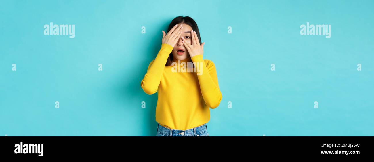 Intrigued asian girl peeking through fingers at something interesting ...