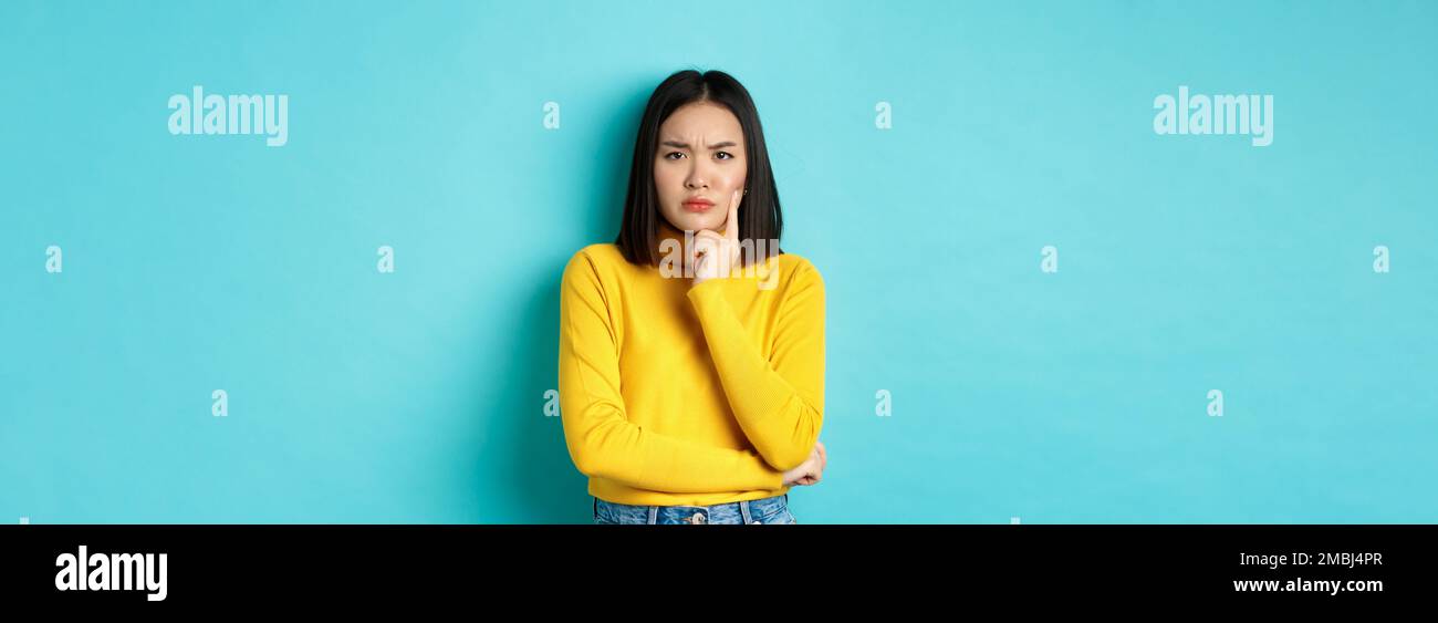 Image of pensive and serious asian woman touching chin, frowning and ...