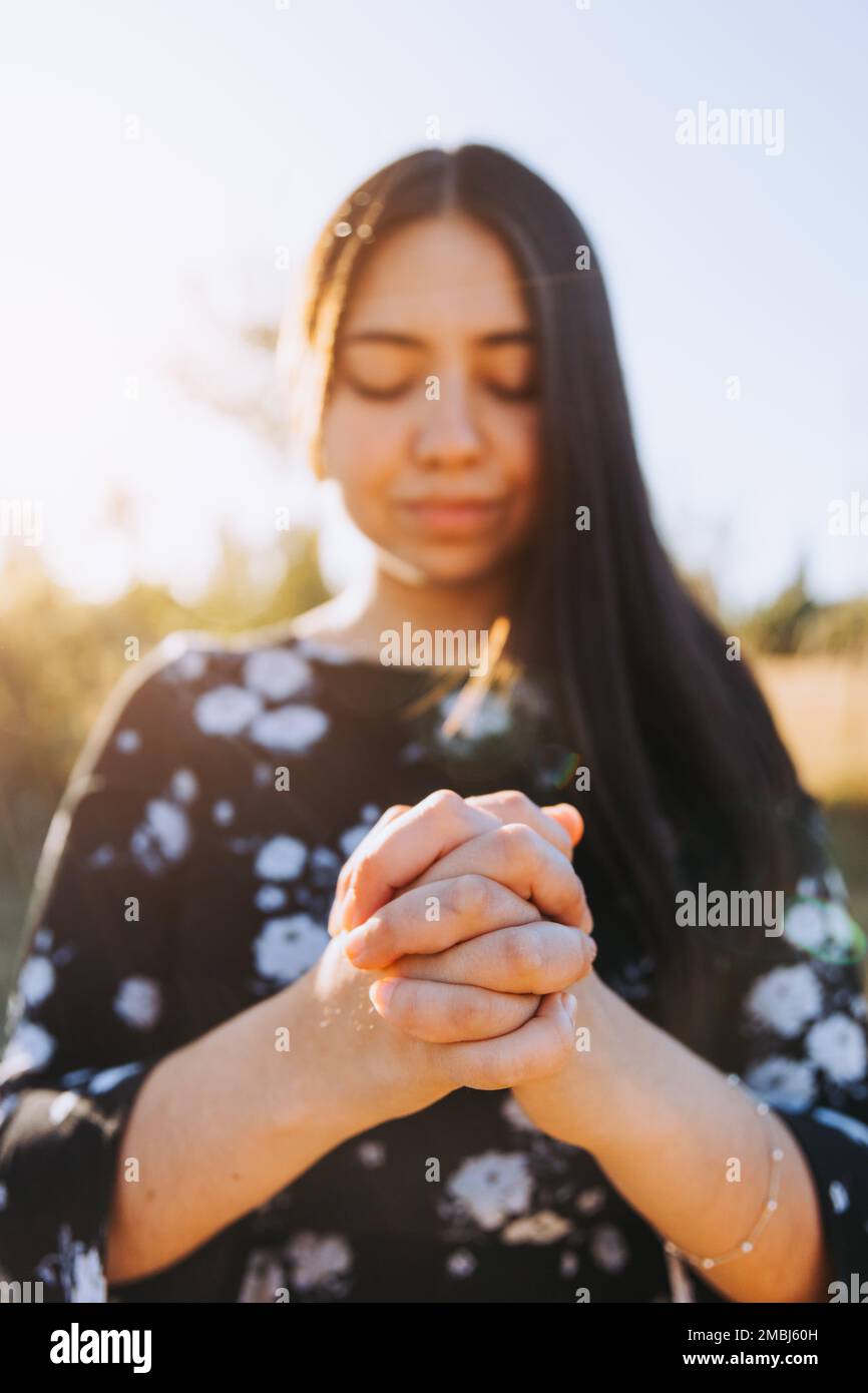 Young believer woman person with praying hands at sunset in the field ...