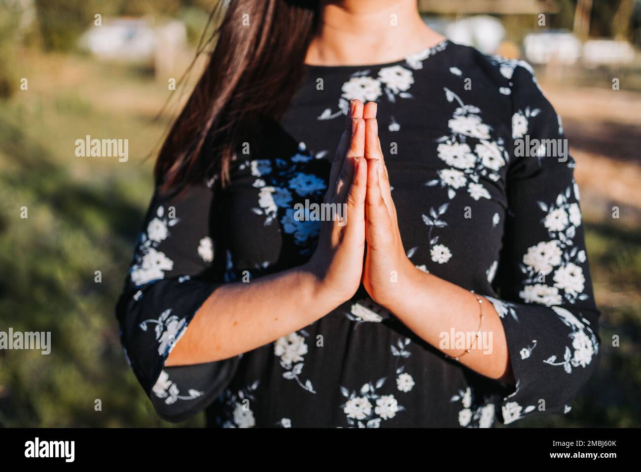 Unrecognizable believer woman with praying hands at sunset in the field ...