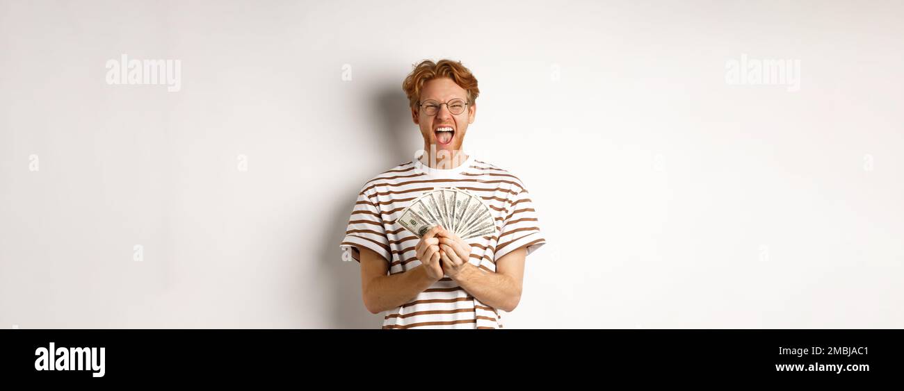 Lucky young man with red hair showing dollars, winning money and ...