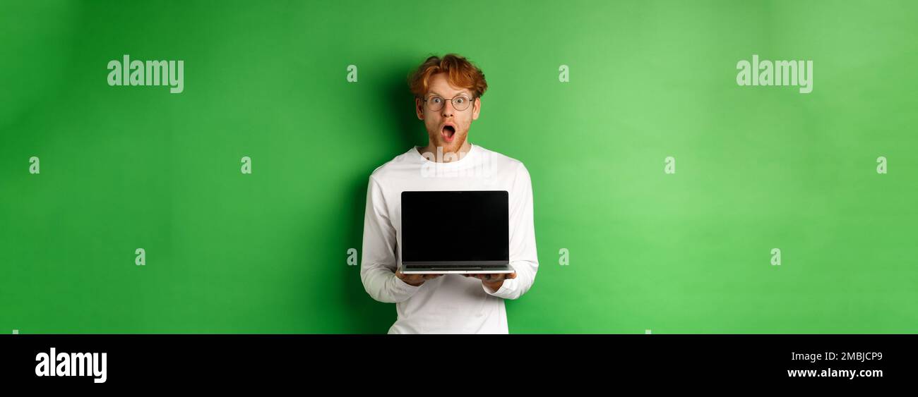 Surprised redhead man in glasses showing laptop blank screen, showing ...