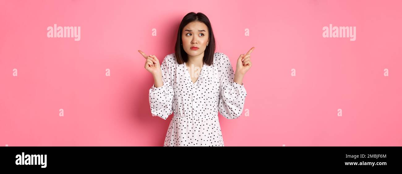 Confused asian woman hesitating, shrugging and pointing hands two sides ...