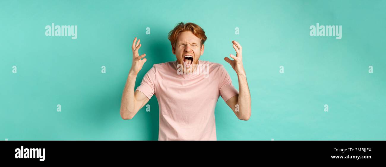 Angry young redhead man screaming distressed, shaking hands and looking ...