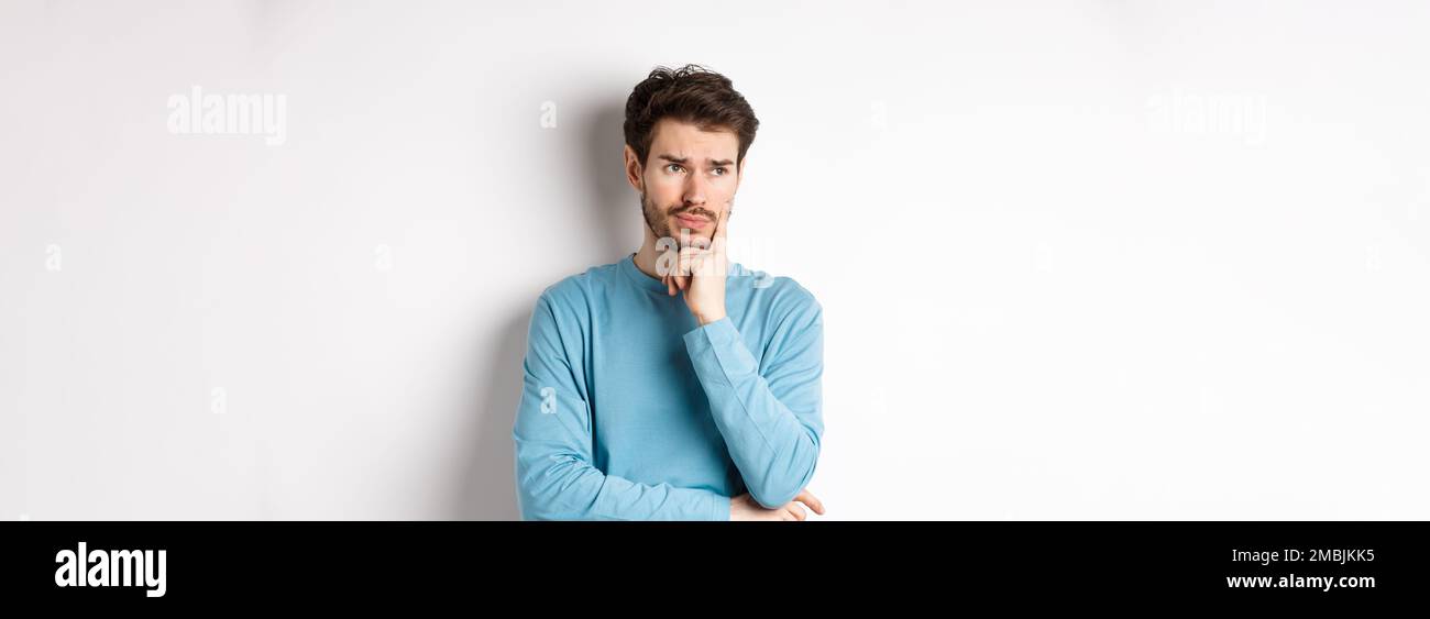 Young bearded man looking pensive and frowning, thinking about problem ...