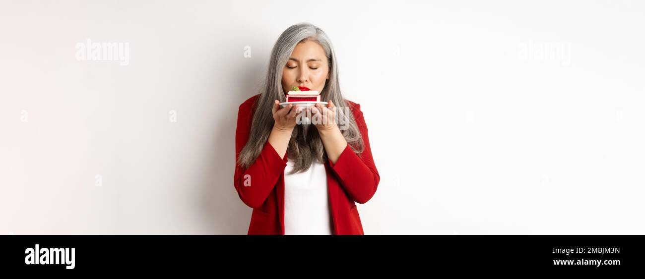 Image of funny asian senior lady sniffing delicious cake, smell dessert ...