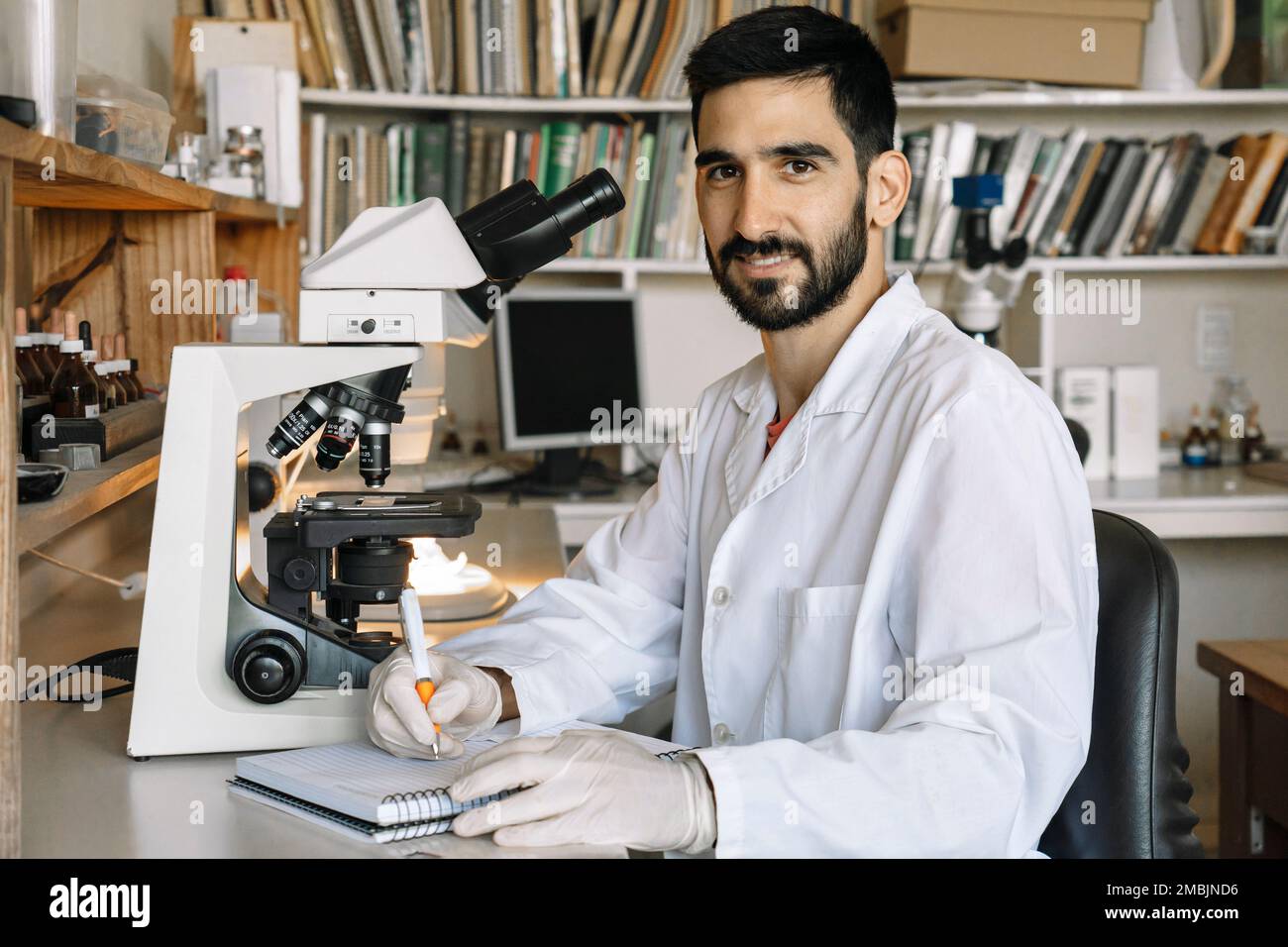 Young scientist in front of microscope, smiles and looks at camera and ...