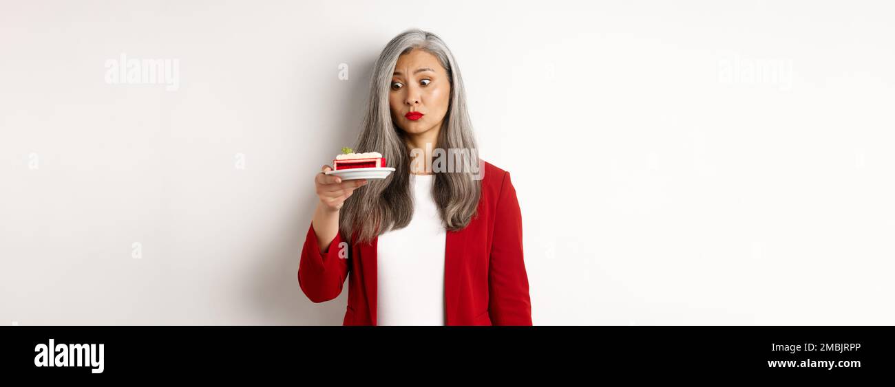 Elegant senior woman in red blazer wants take bite of sweet cake ...