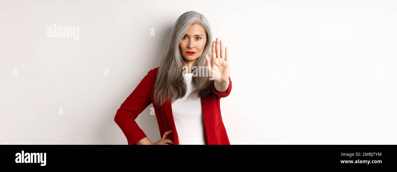Serious asian woman in red blazer showing stop sign, telling no ...