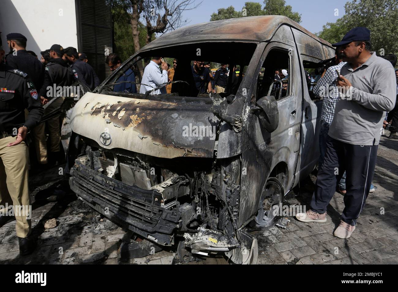 Pakistani police officers and investigators examine a burned van at the ...