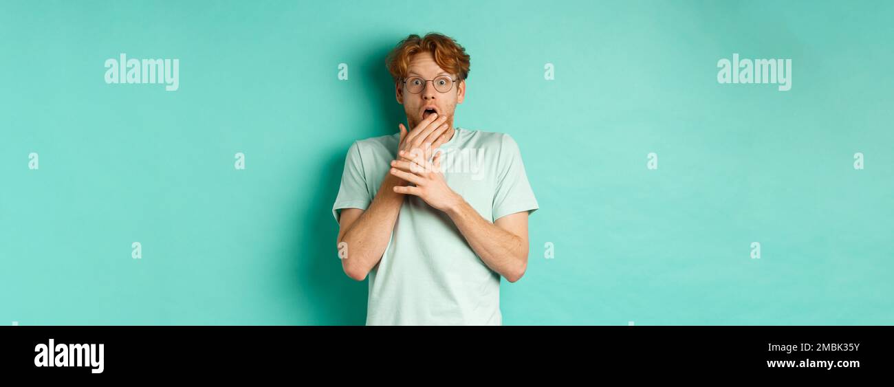 Shocked redhead man in glasses gasping startled, covering mouth and ...