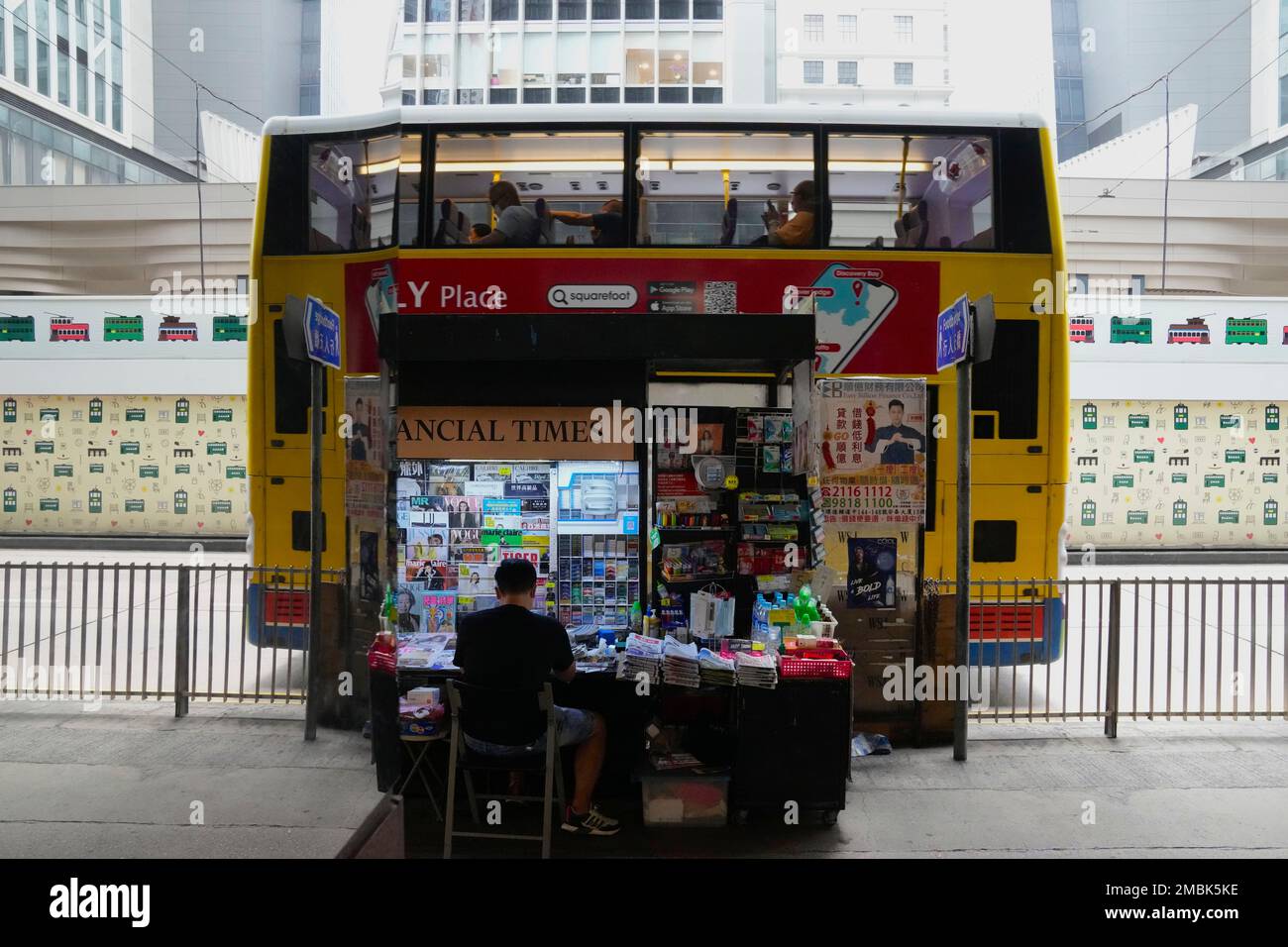 A newsstand vendor reads newspaper as passengers wearing masks ride in ...