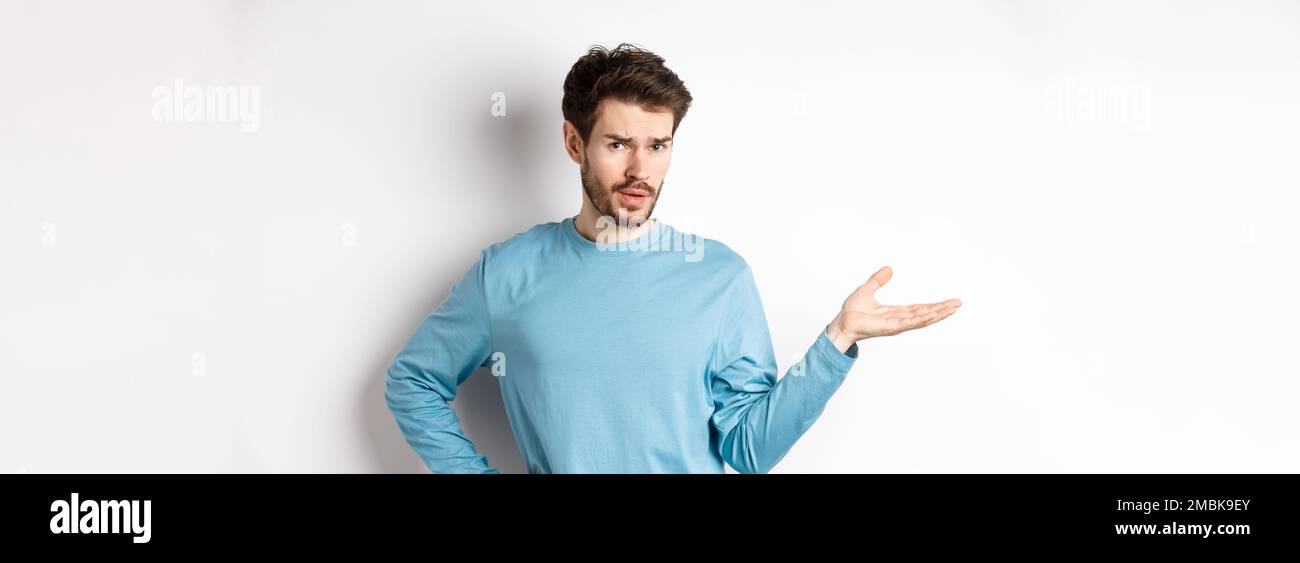 So what. Confused young man raising hand and looking skeptical at ...