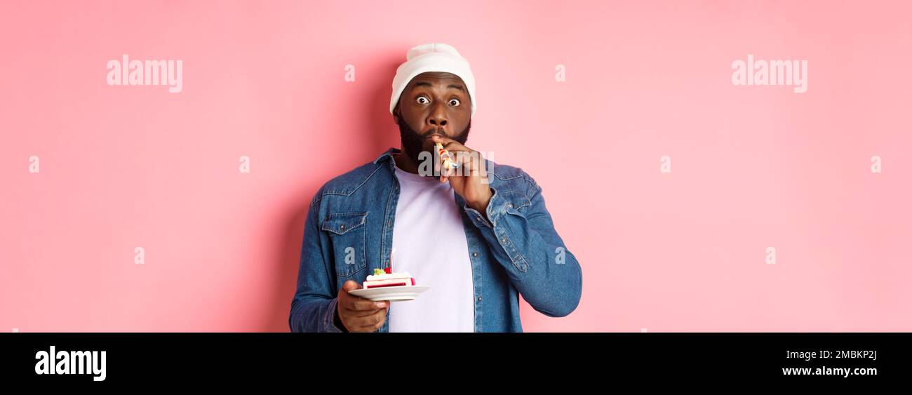 Happy Black hipster celebrating birthday, blowing party whistle ...