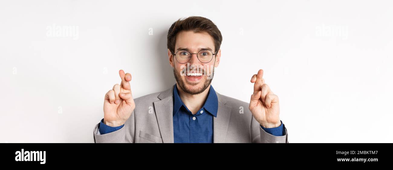 Close-up of hopeful male entrepreneur in glasses and suit cross fingers ...