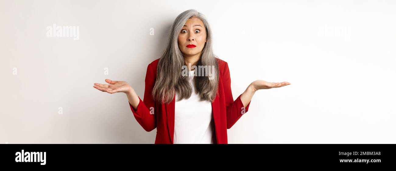Confused asian senior woman shrugging, spread hands sideways and ...