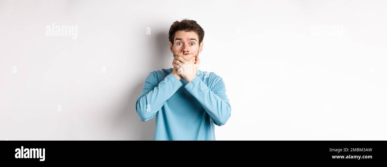 Image of shocked young man staring startled and covering mouth with ...