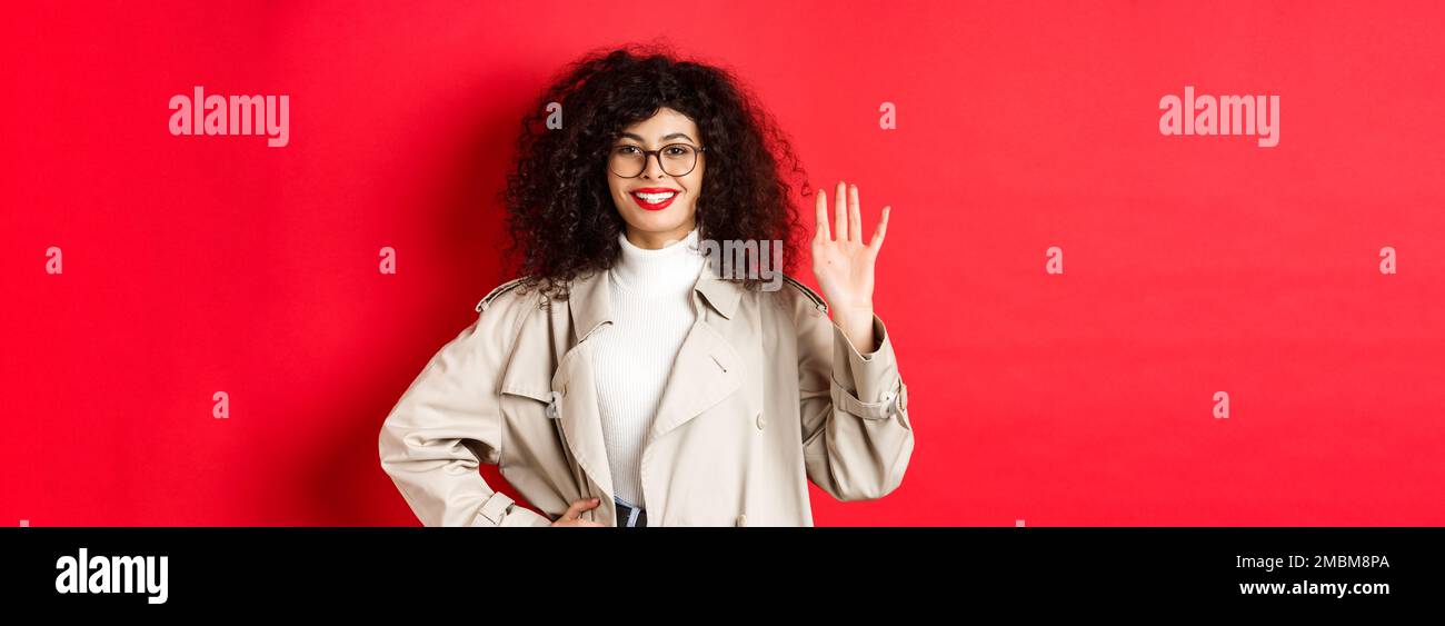 Stylish european woman in glasses and trench coat, waiving hand and ...