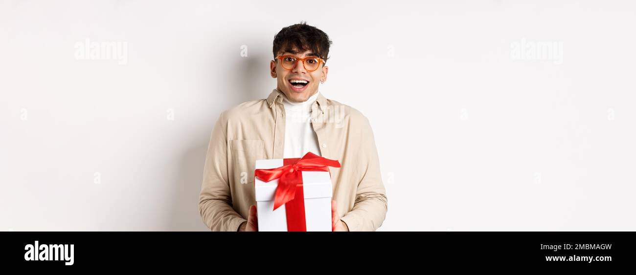 Surprised happy guy receiving a gift, holding present box and smiling ...