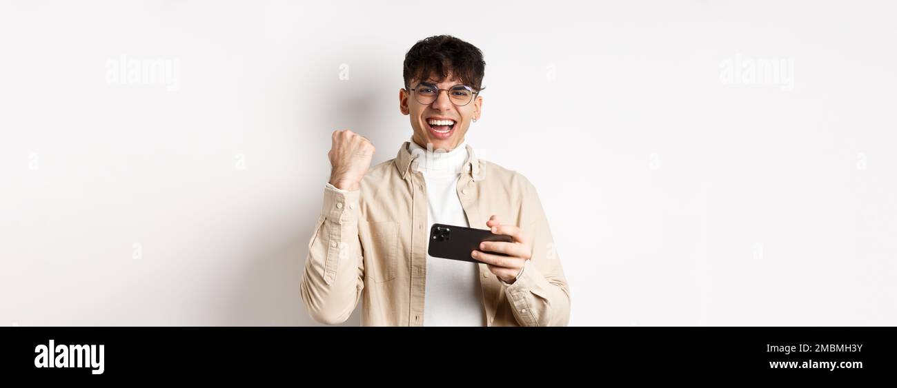 Happy guy winning on smartphone, holding mobile phone and raising hand ...