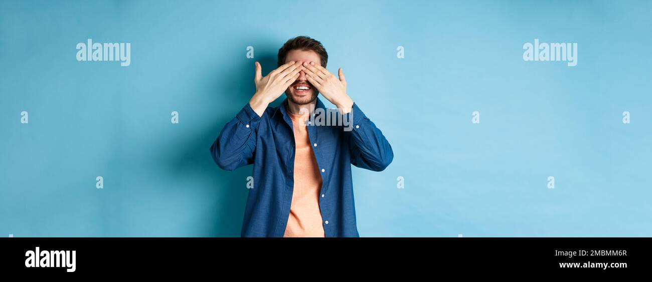 Happy smiling guy waiting for surprise, covering eyes with hands and ...