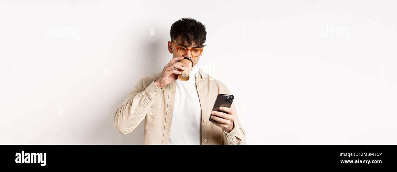 Real people. Young man reading smartphone screen and drinking coffee ...