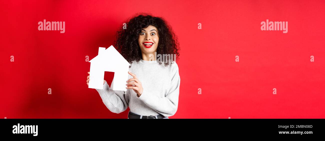 Real estate. Excited smiling woman showing paper house cutout and ...