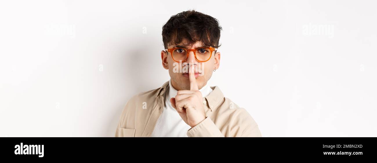 Close-up of grumpy young guy in glasses frowning and shushing, make ...