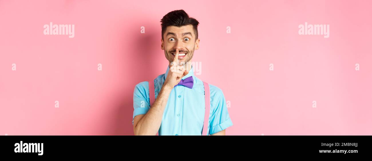 Cheerful young man making surprise, shushing at camera with happy smile ...