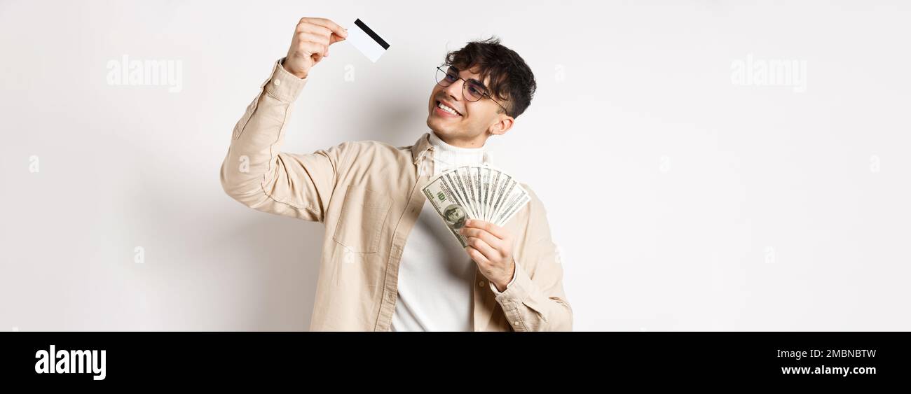 Satisfied young guy holding money, looking pleased and smiling at ...